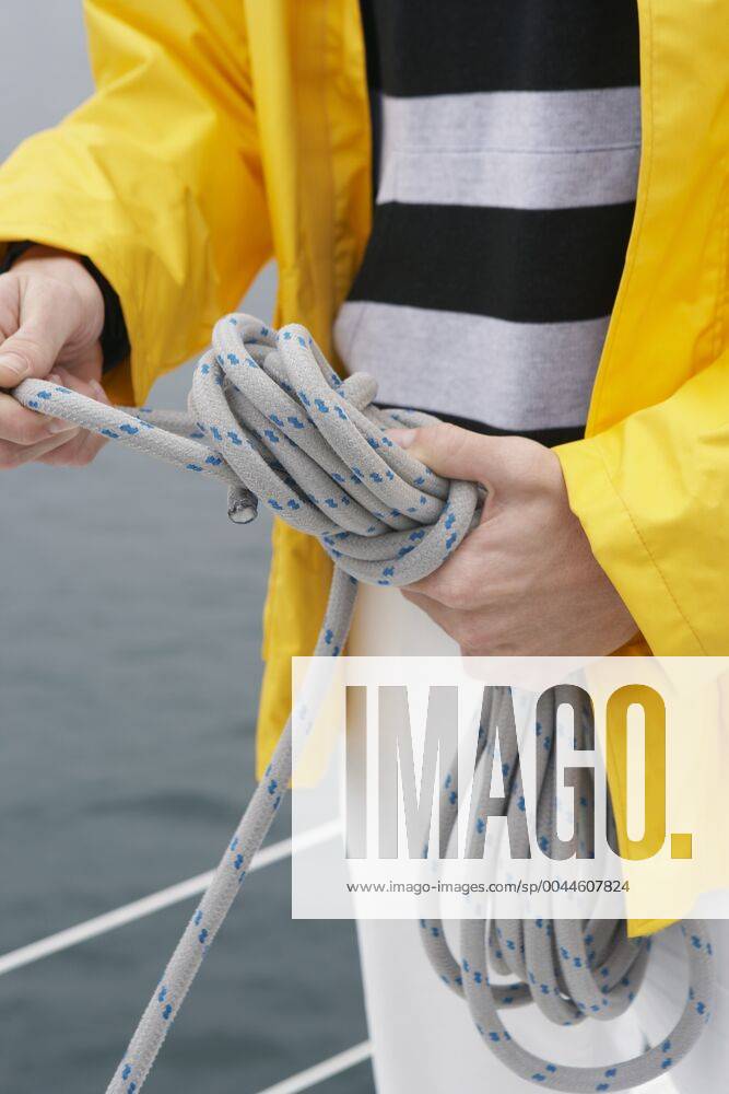 Young man tying rope on yacht, mid section
