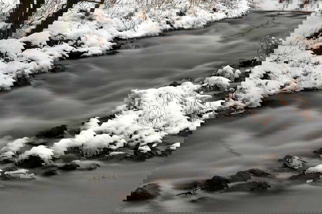 Der Fluss Ilm in Thüringen mit verschneiten Ufern wirkt durch ...