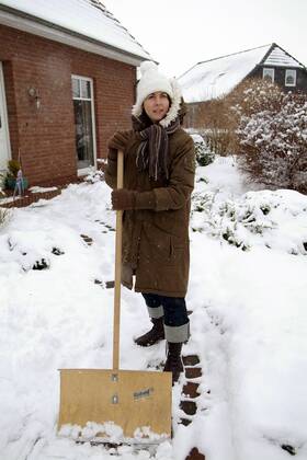 Frau räumt mit Schippe den Schnee vom