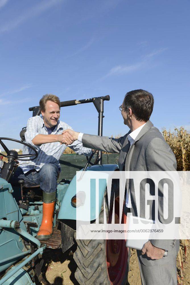 Farmer welcomes businessman with handshake while sitting on a tractor ...