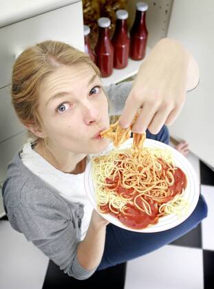 Junge Frau sitzt auf einem Schrank und isst Spaghetti . Berlin ...