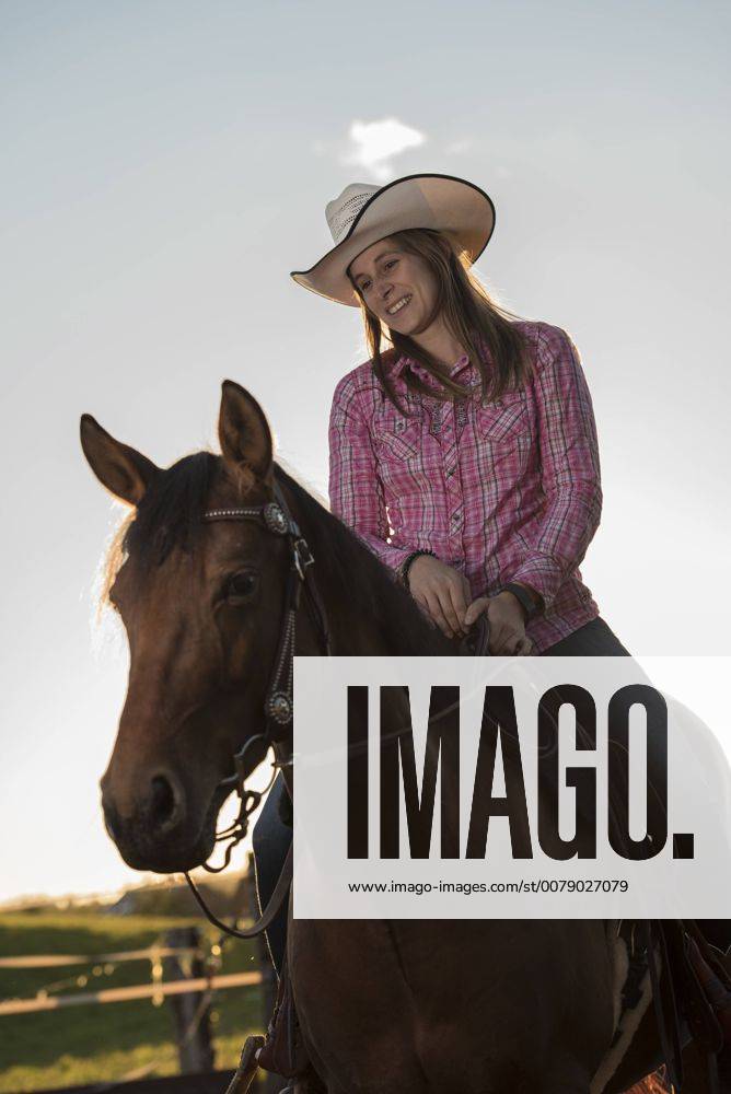 Lächelnd blickt eine junge im Westernstil reitende Frau auf Ihr Pferd ...