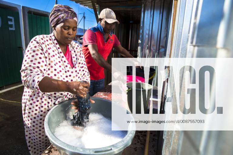 A woman washes clothing in a shallow bucket of water in Asanda Village ...