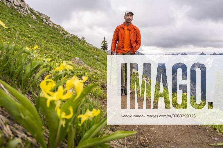 A man hiking past avalanche lilies in front of the Early Winter Spires ...