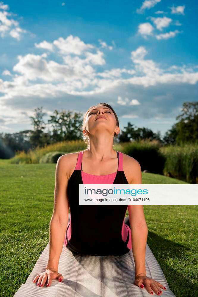 Relaxed young woman practicing cobra yoga pose in park ...