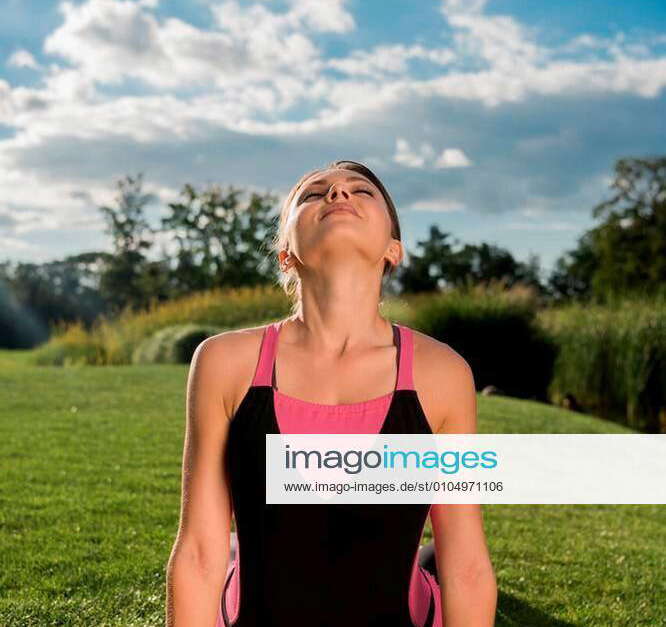 relaxed young woman practicing cobra yoga pose in park ...