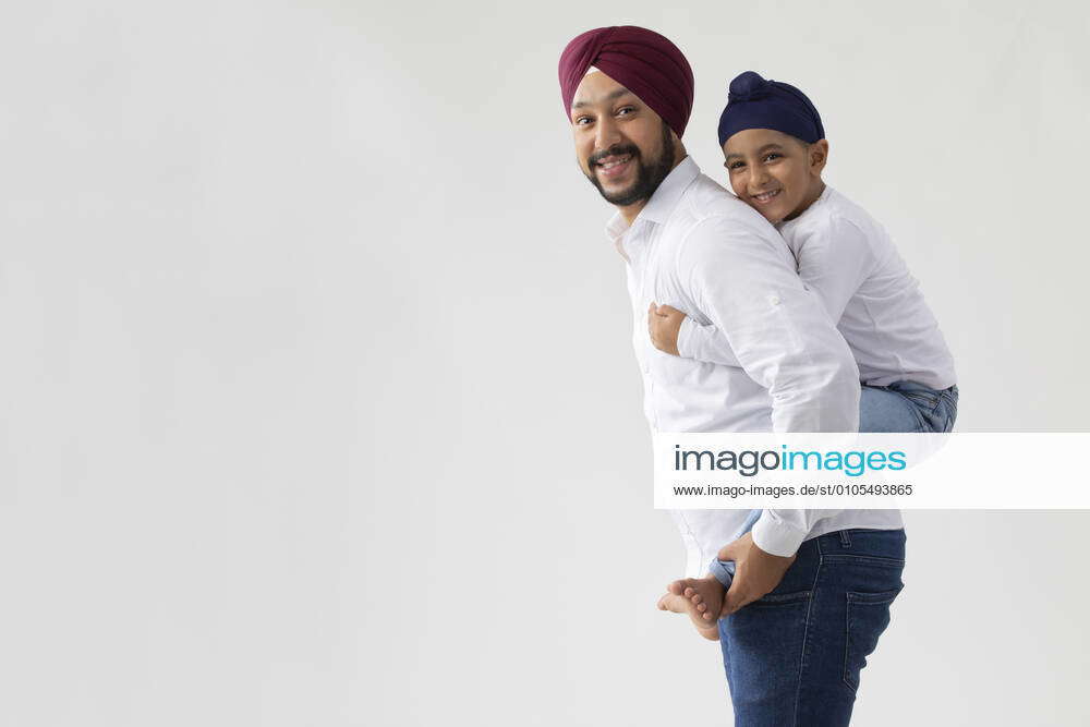 A SIKH FATHER CARRYING HIS SON ON HIS BACK SIMILING AND POSING PRZH
