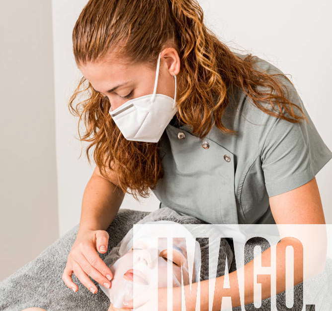 Cosmetician in protective mask applying facial cloth mask on female ...