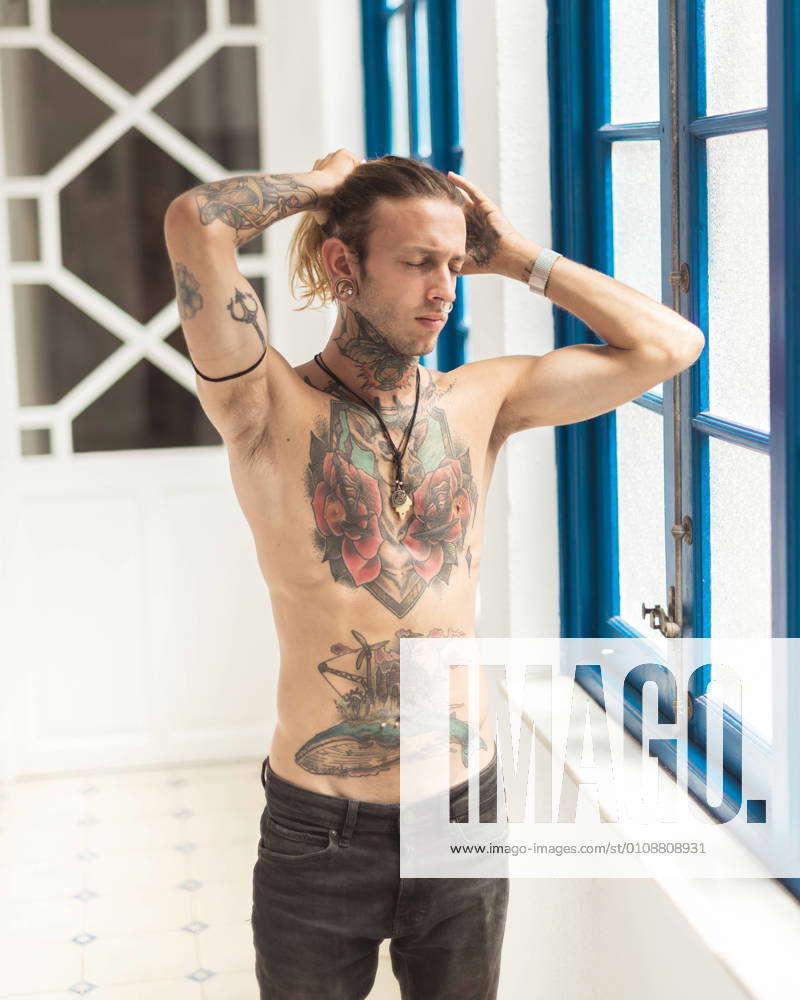 Handsome young slender man with tattooed torso standing and looking ...