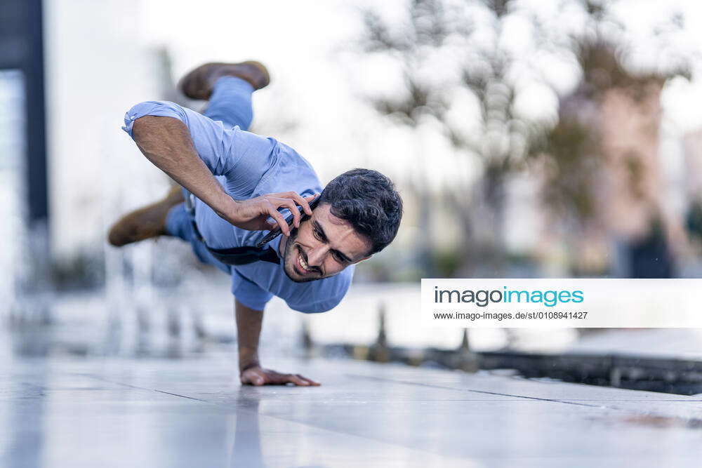 Smiling businessman talking on mobile phone while doing handstand on ...