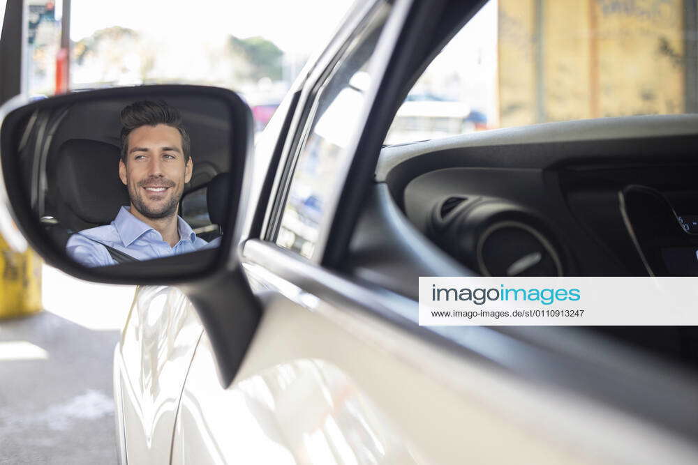 Wing mirror reflection of businessman smiling while driving car model ...