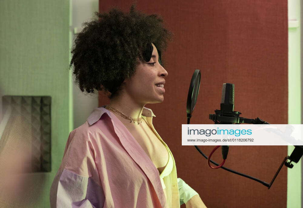 Black female singer performing song against microphone with pop filter ...