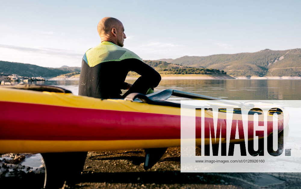 Back view of serene thoughtful male surfer with paddle sitting looking ...