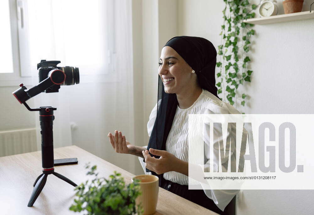 Smiling female vlogger talking while filming through camera at home ...