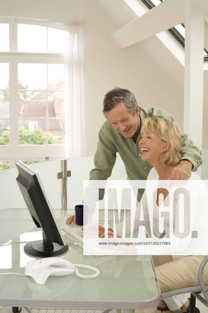 Couple using computer and laughing at home desk