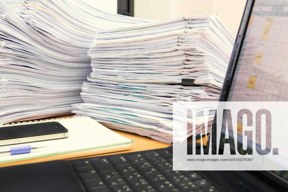 Computer notebook and documents on desk stack up high waiting to be managed
