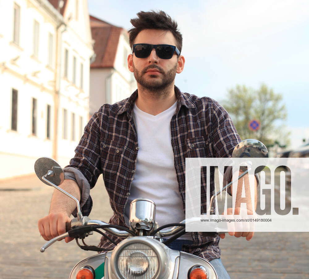 Fashionable young man riding a vintage scooter in the street ...