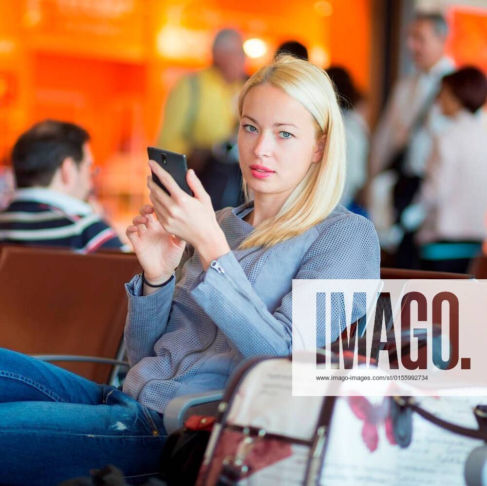 Casual Blond Young Woman Using Her Cell Phone While Waiting To Board A