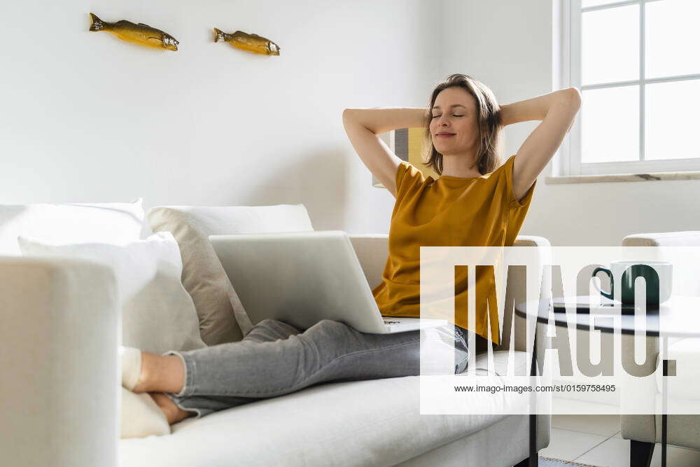 Smiling Woman With Hands Behind Head Sitting On Sofa In Living Room