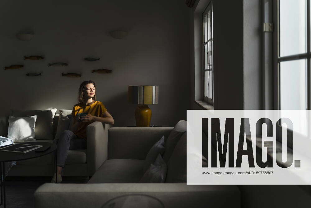 Woman With Eyes Closed Sitting On Sofa In Dark Living Room Model