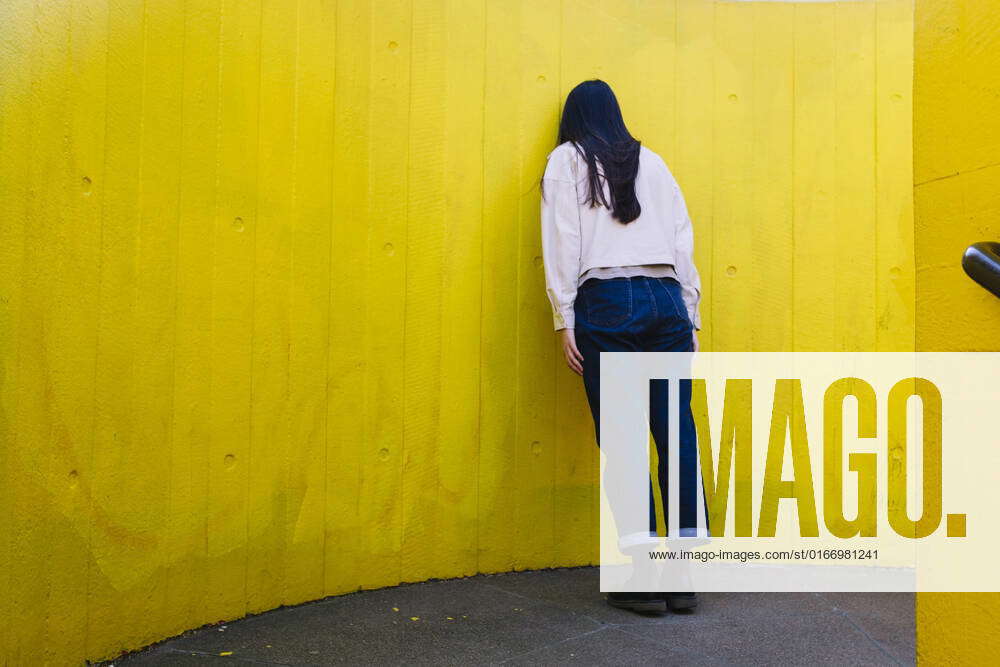 Depressed young woman leaning on yellow wall model released, Symbolfoto