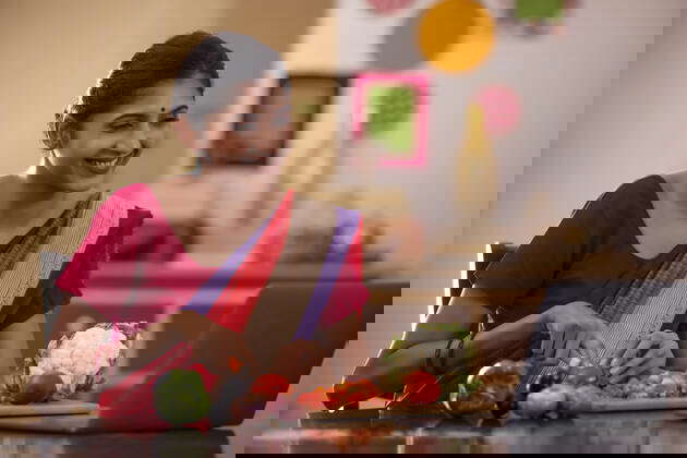 Smiling woman having video call while chopping vegetables at home