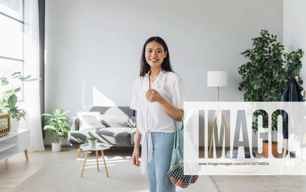Smiling Woman Carrying Mesh Bag With Vegetables In Living Room Model