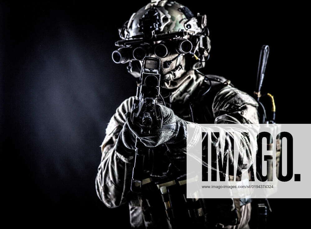 Soldier aiming assault rifle with collimator sight at camera, low key ...