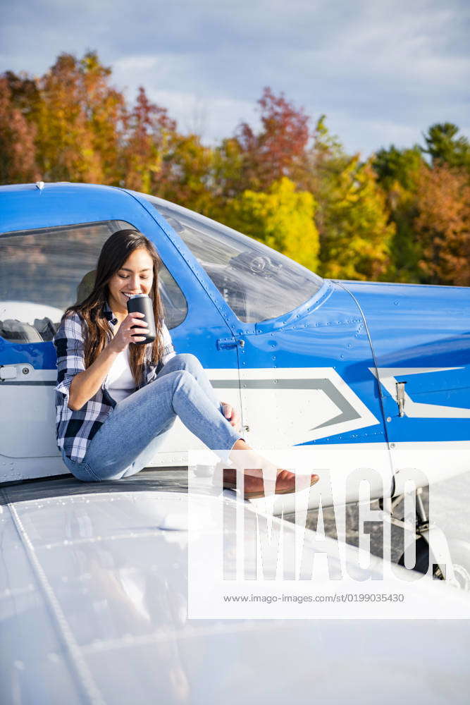 Young BIPOC Female Pilot sipping morning coffee on small plane wing ...