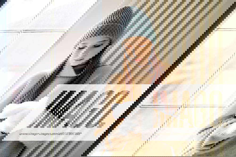 Teenage girl wearing mittens and knit hat standing in front of radiator ...