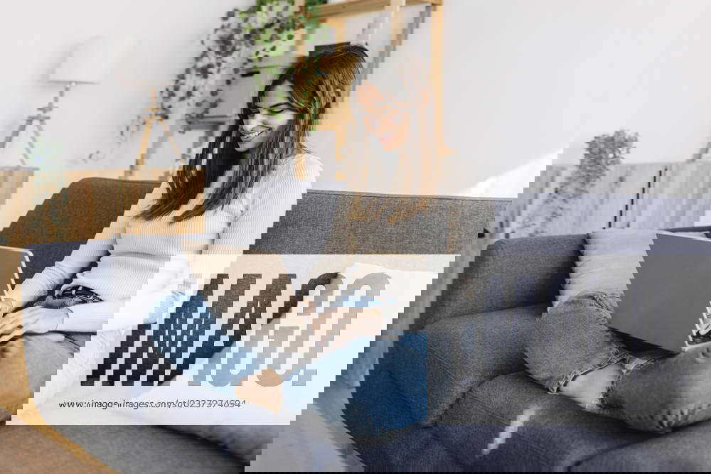 Happy Woman Using Laptop Sitting On Sofa In Living Room Model Released