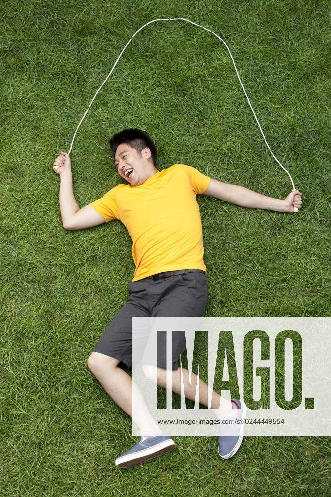 Creative young Chinese man imitating jumping rope on meadow Beijing