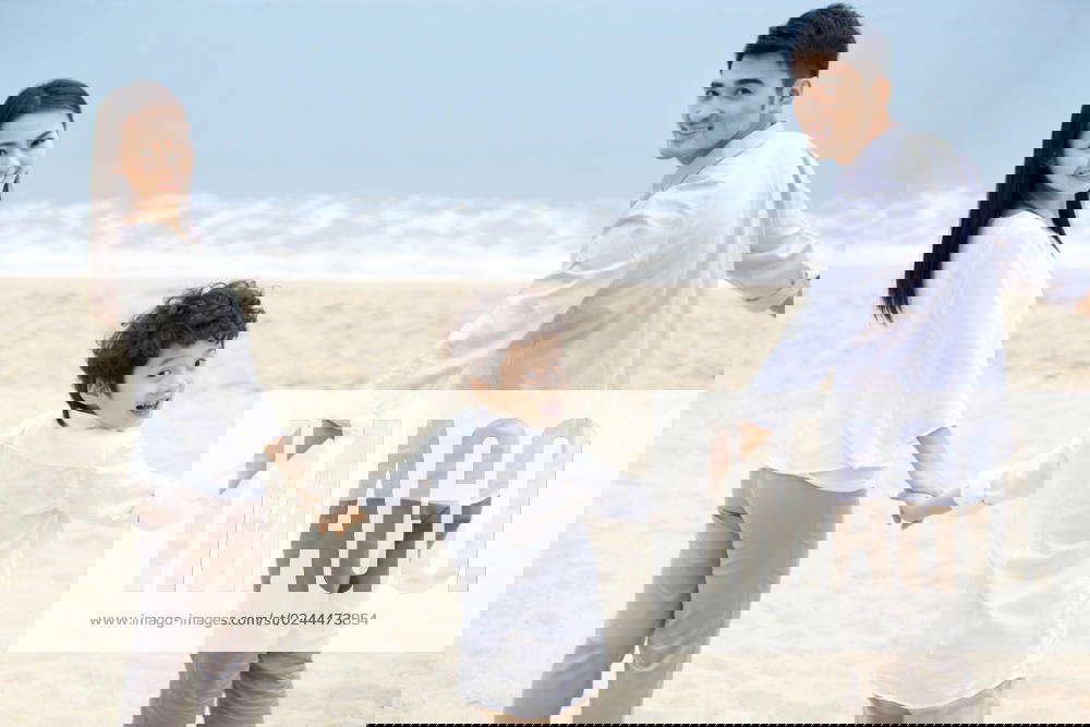 Happy young Chinese family looking back hand in hand on the beach of ...