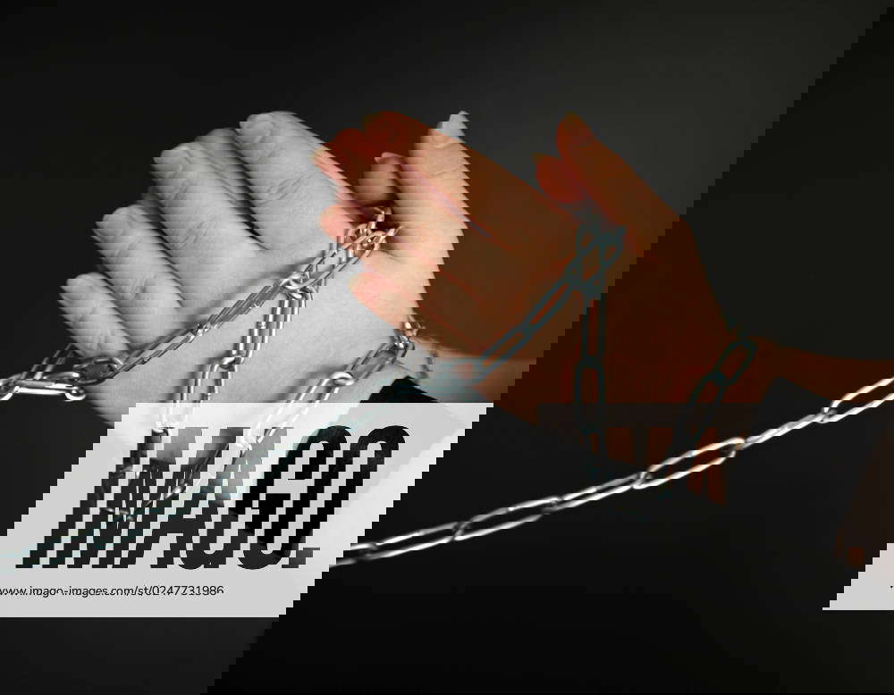 Women s hands shackled a metal chain on a dark background