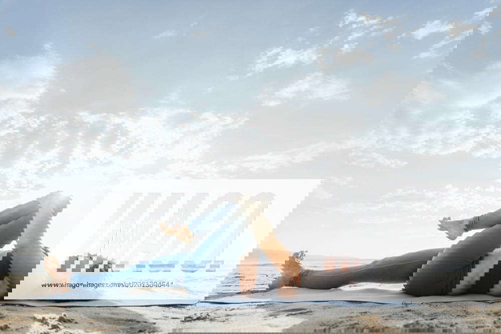 Woman stretching leg lying down on exercise mat at beach model released ...