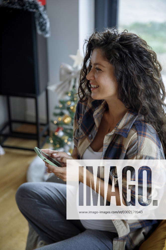 Smiling Pregnant Woman With Smart Phone In Living Room Model Released