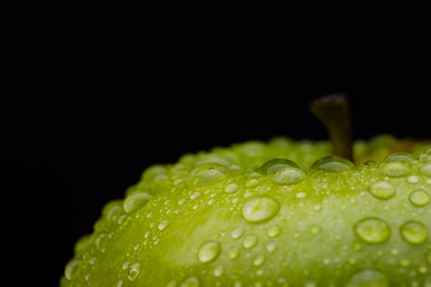 Micro close up of green apple with water drops and copy space on black ...