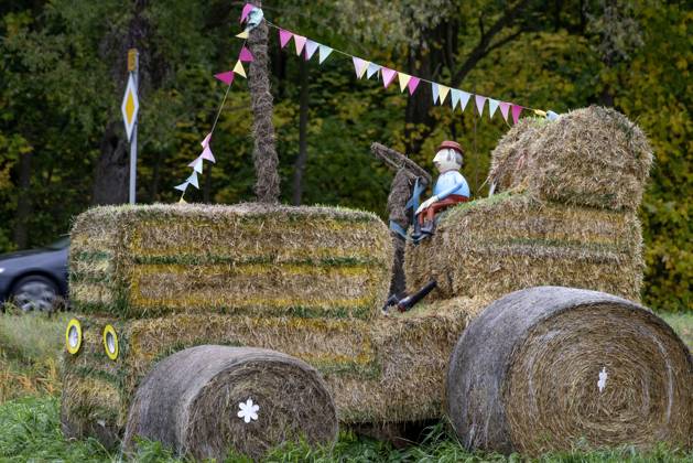 A man made of papier mâché sits on a tractor made of straw ...