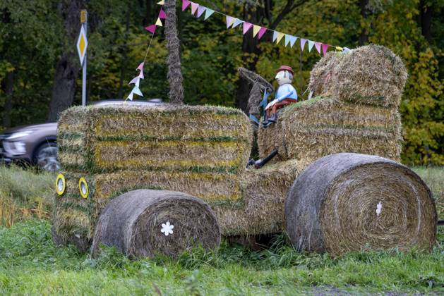 A man made of papier mâché sits on a tractor made of straw ...