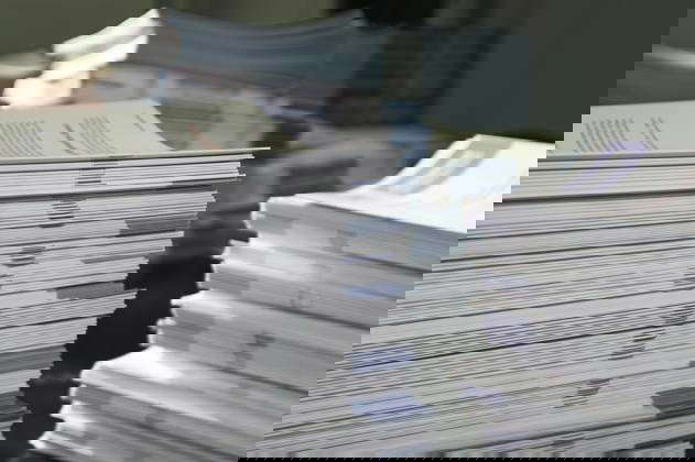 Computer notebook and documents on desk stack up high waiting to be managed