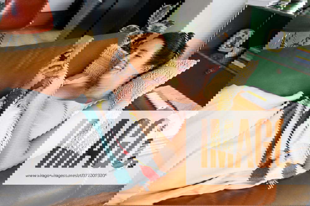 Happy woman using smart phone while lying down on sofa at home Germany, Berlin, model released