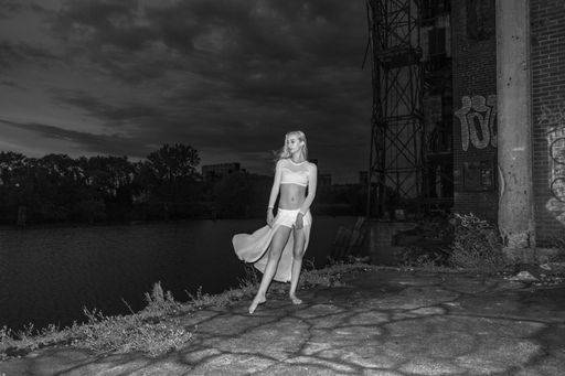 A greyscale of a blonde model posing near a lake surrounded by trees in ...