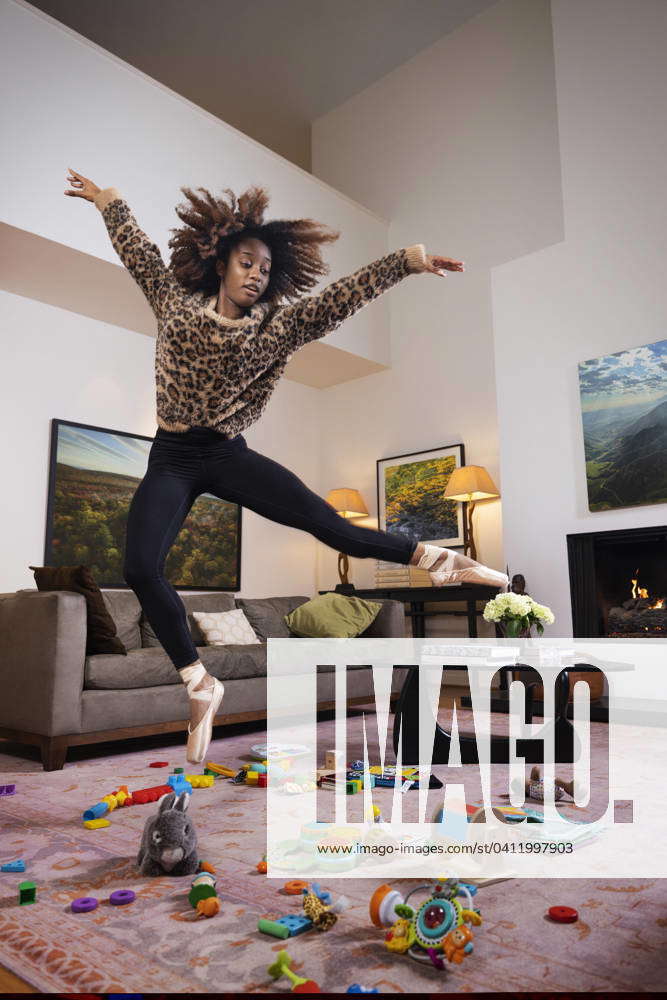 Female ballet dancer jumping over sea of toys in a living room. Dallas ...