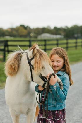 Young girl walks her white miniature pony in green field at barn ...