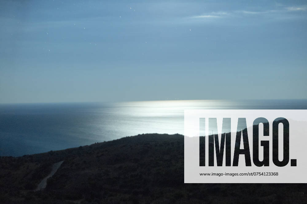 Moonlight reflects over a calm sea beyond a silhouetted coastline under ...