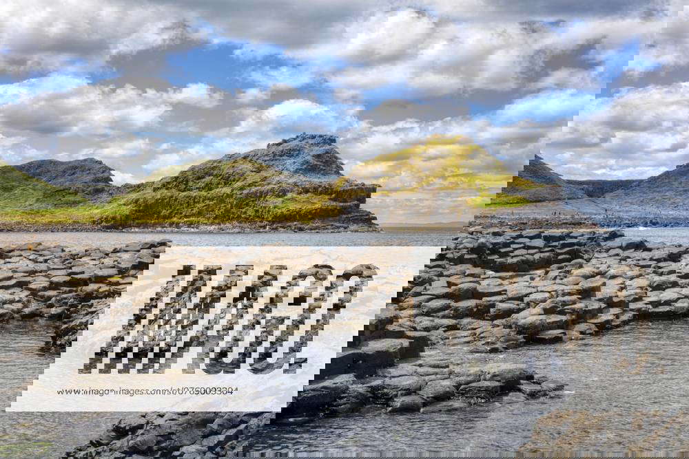 Breite Küstenlandschaft mit grasbewachsenen Hügeln und Felsen im Meer ...