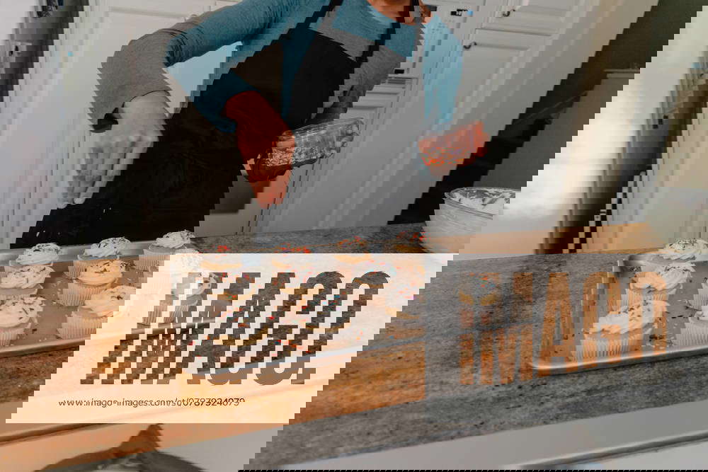 Baker sprinkling rainbow sprinkles to vanilla cupcakes Carlsbad ...